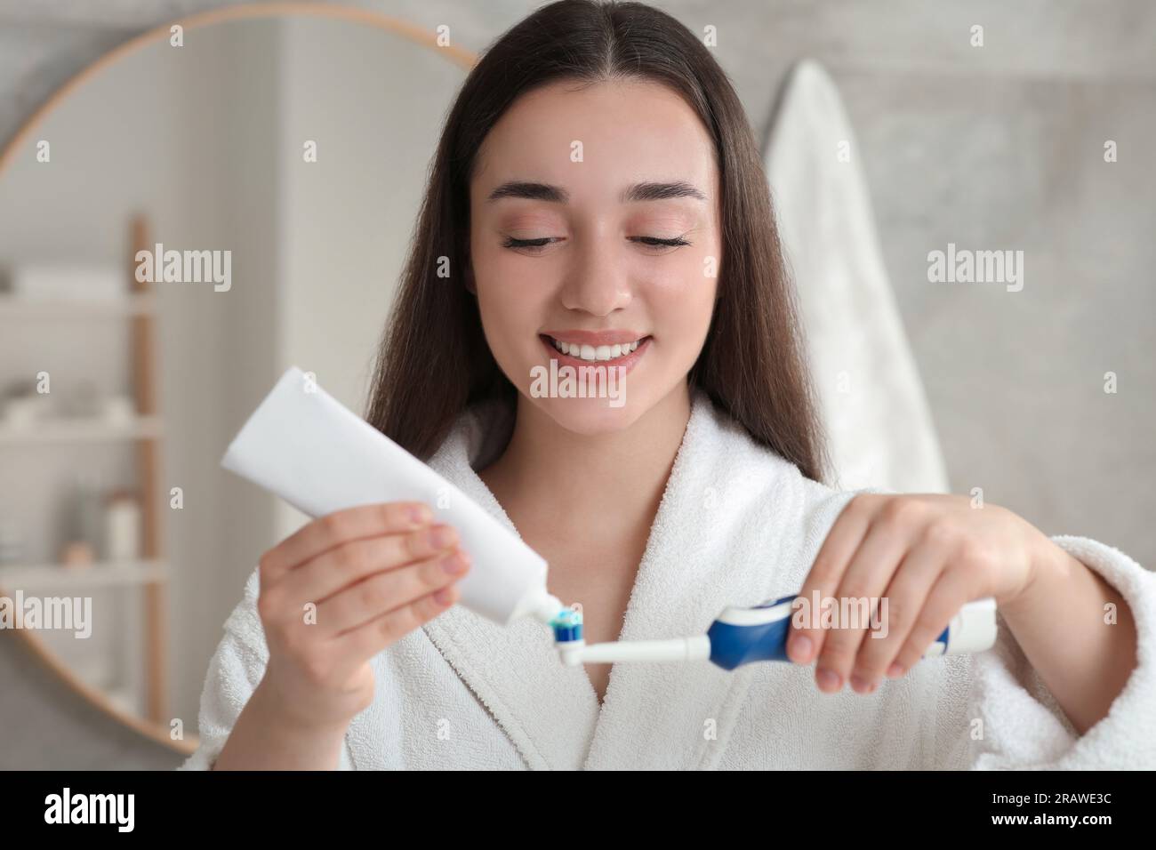 Young woman squeezing toothpaste from tube onto electric toothbrush in ...