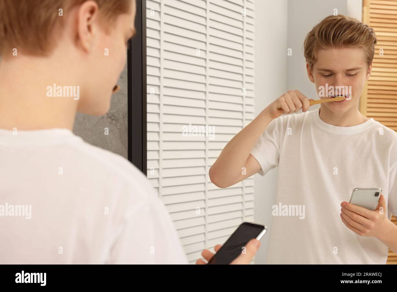 Teenage boy using smartphone while brushing teeth in bathroom. Internet ...