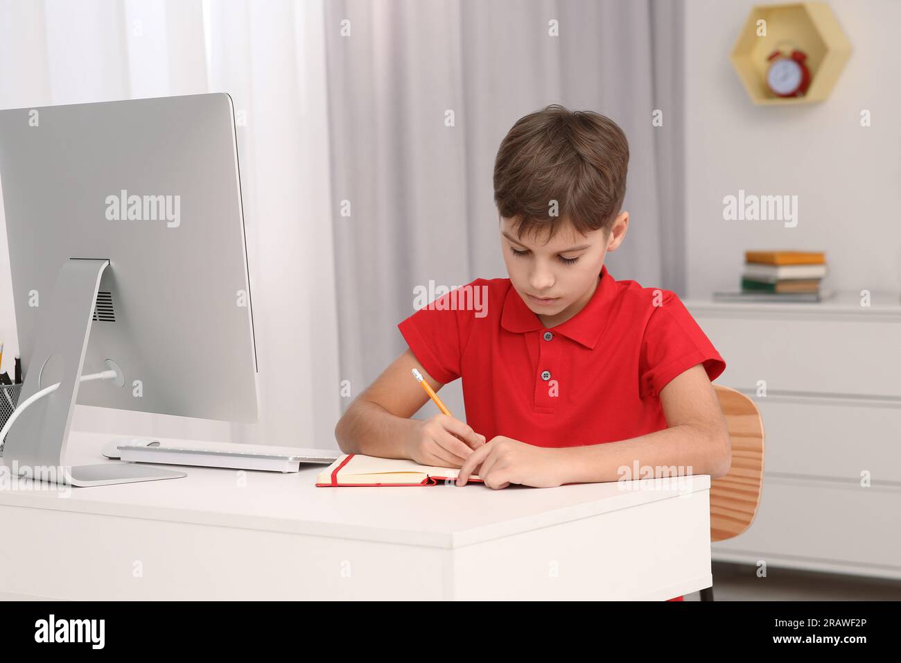 Boy writing in notepad while using computer at desk in room. Home ...
