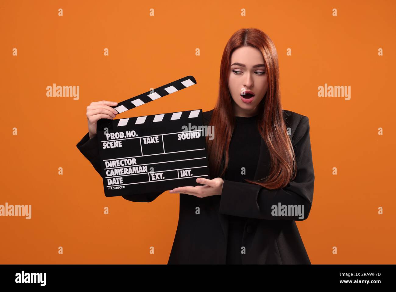 Shocked actress with clapperboard on orange background. Film industry ...