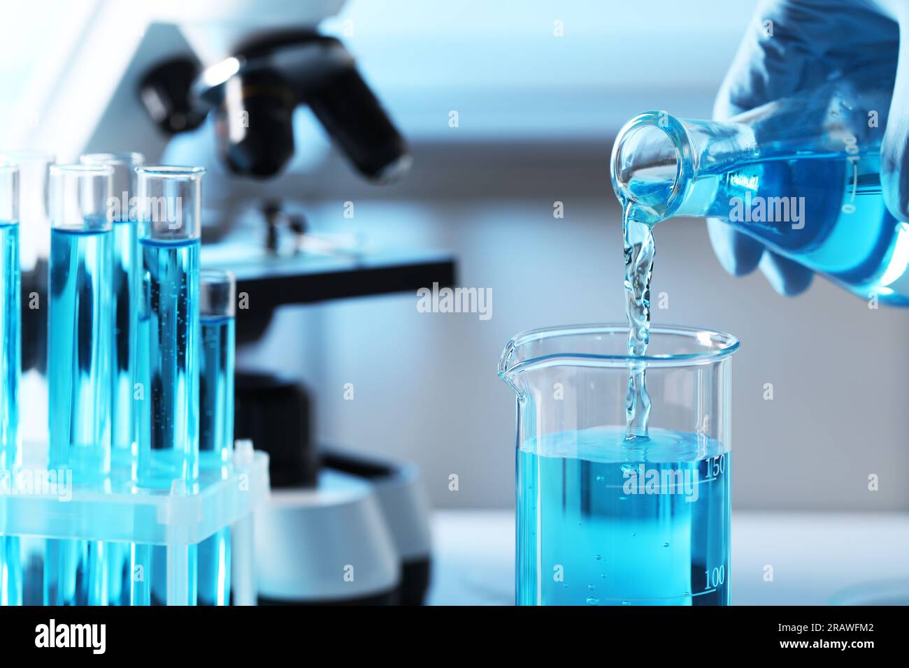 Scientist pouring light blue liquid from flask into beaker near test ...