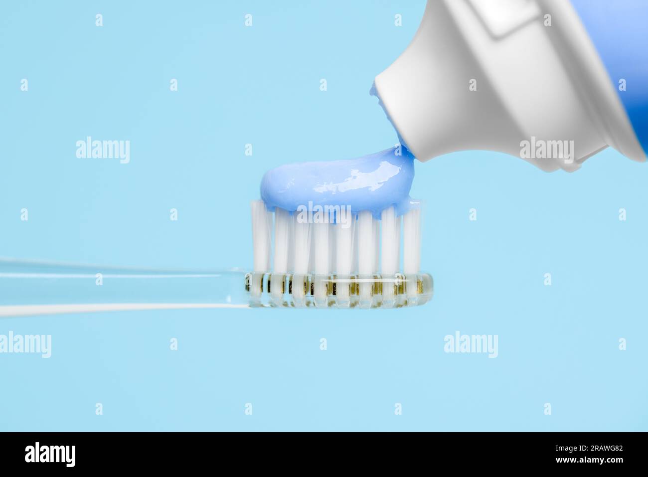 Squeezing toothpaste onto electric toothbrush on light blue background ...
