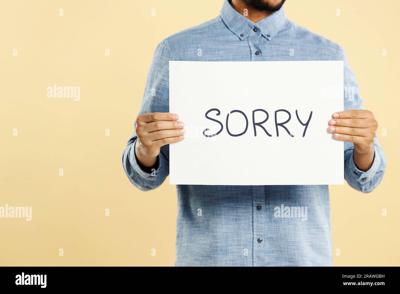 Apology. Man holding card with word Sorry on beige background, closeup ...
