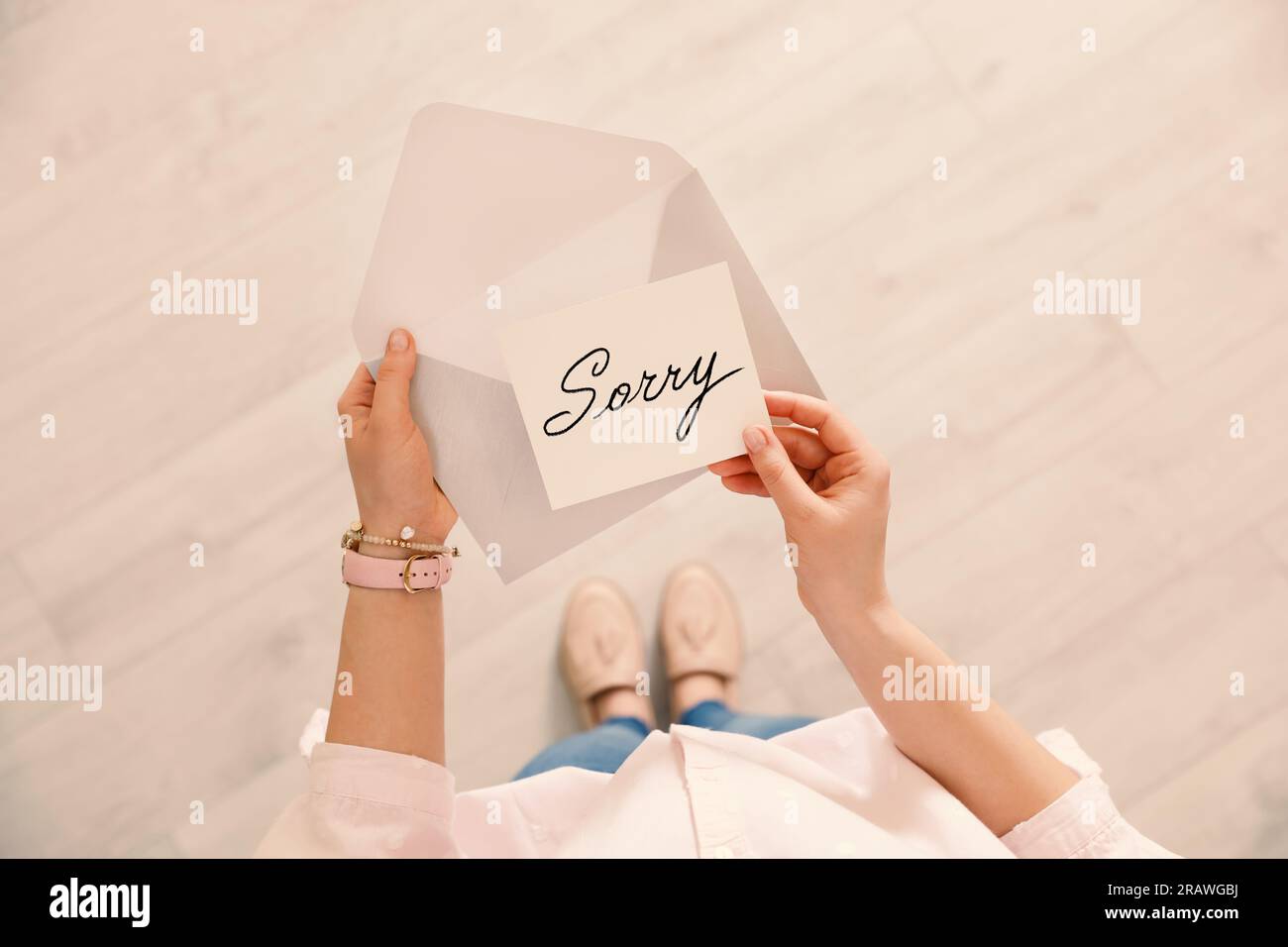 Woman receiving apology message indoors, top view. Card with word Sorry ...