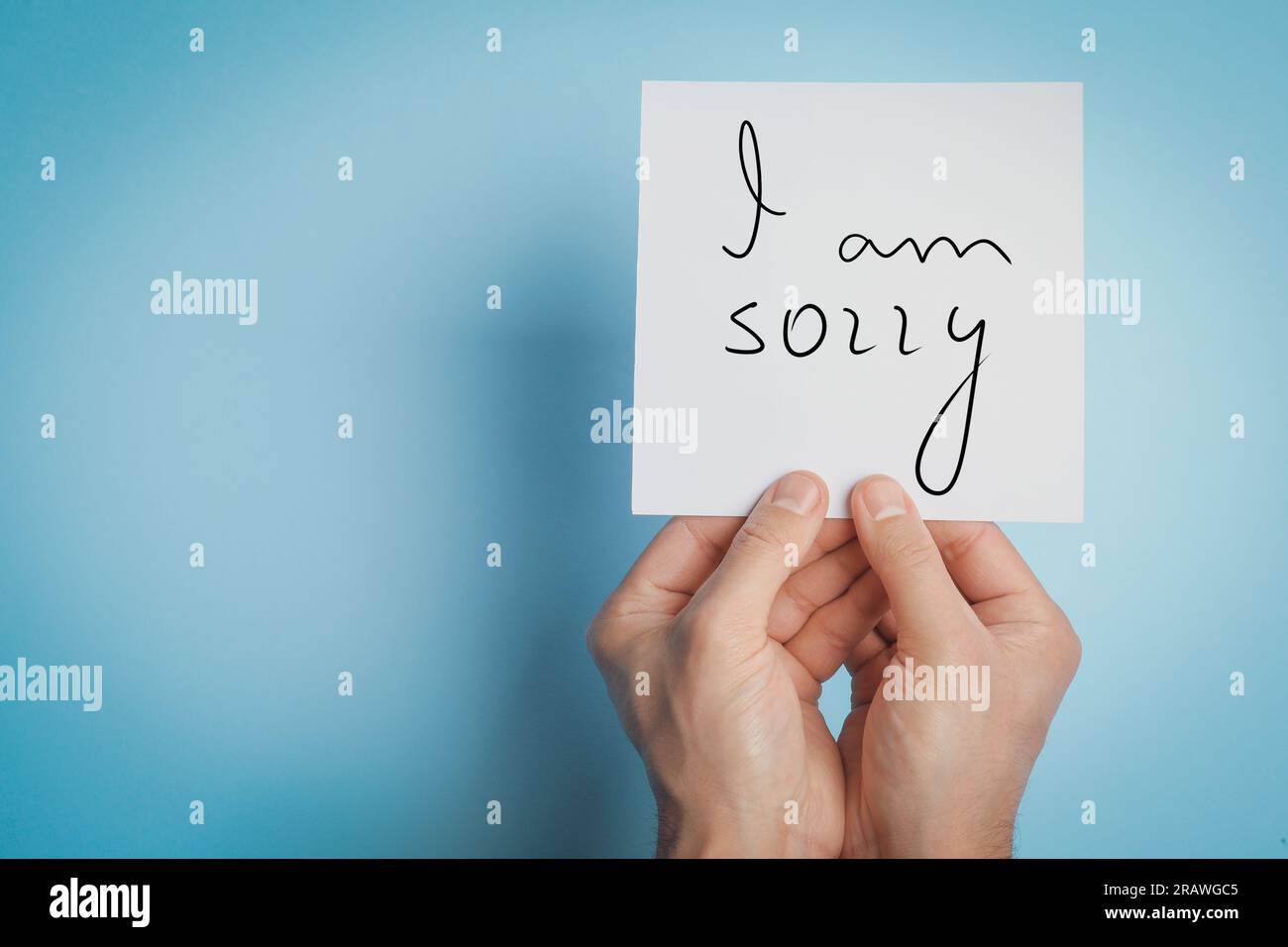 Apology. Man holding card with phrase I Am Sorry on light blue ...