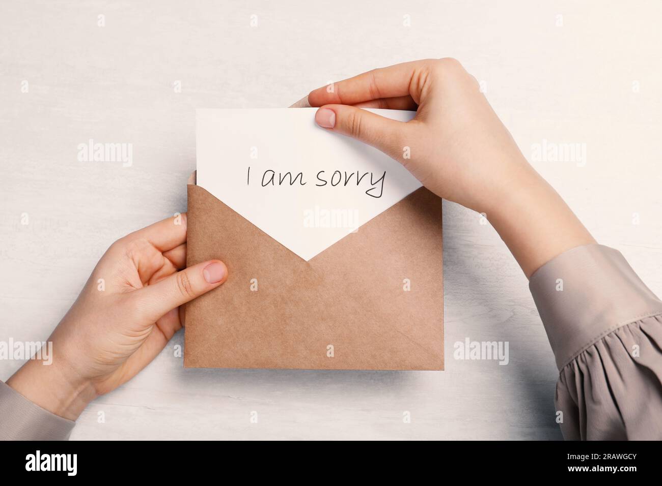 Apology. Woman taking card with word Sorry out of envelope at light ...