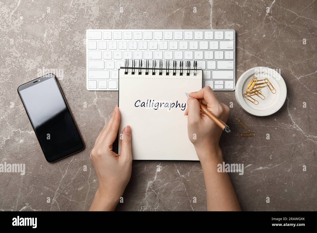 Woman writing word Calligraphy in notebook at grey marble table, top ...