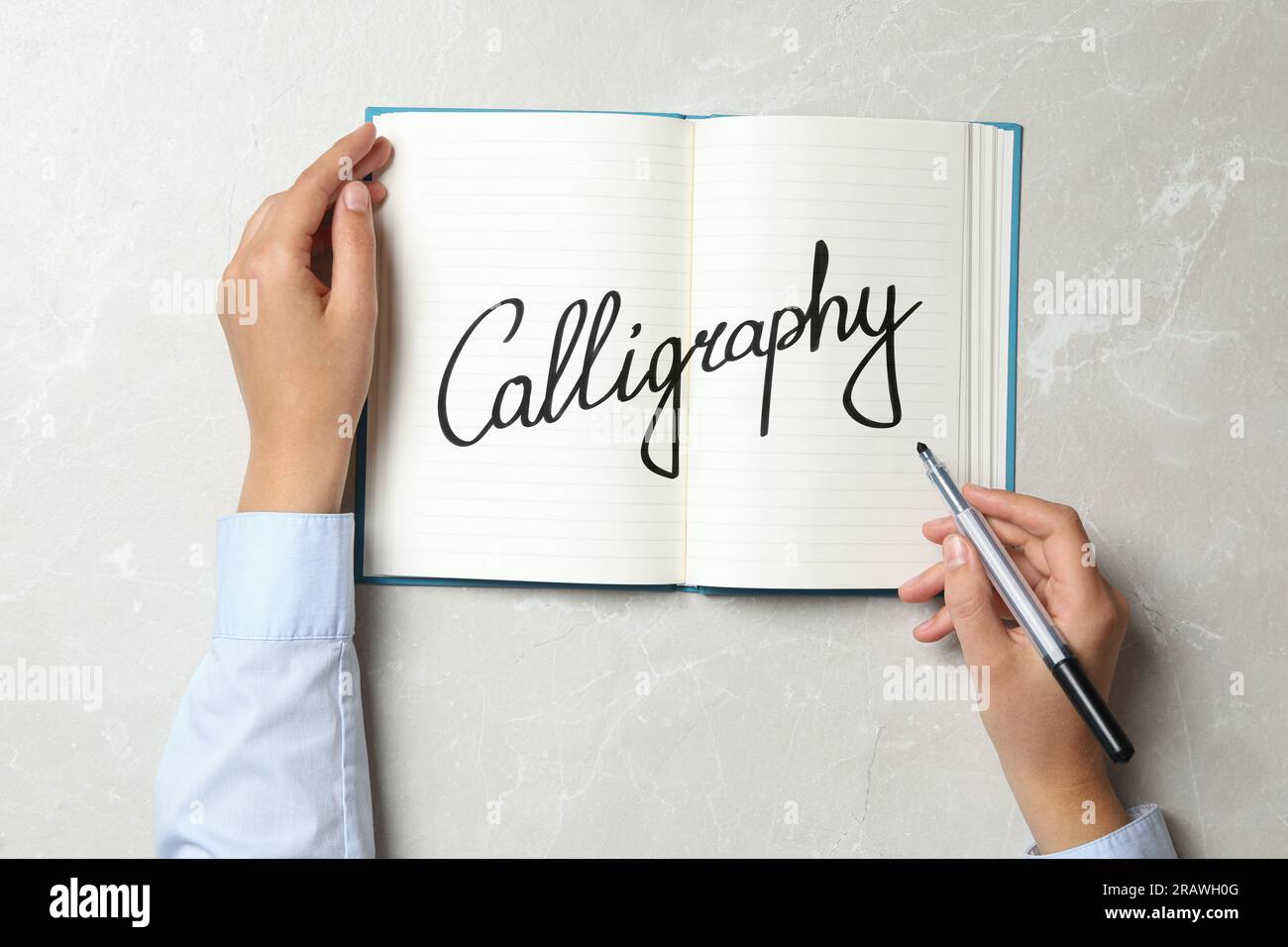 Woman writing word Calligraphy in notebook at marble table, top view ...