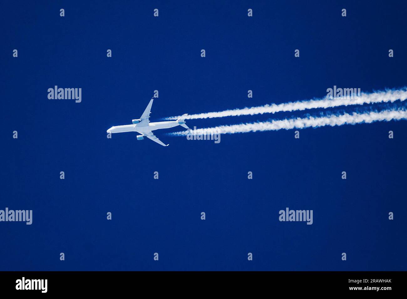 Sharp telephoto close-up of jet plane aircraft with contrails cruising from Doha to San ...