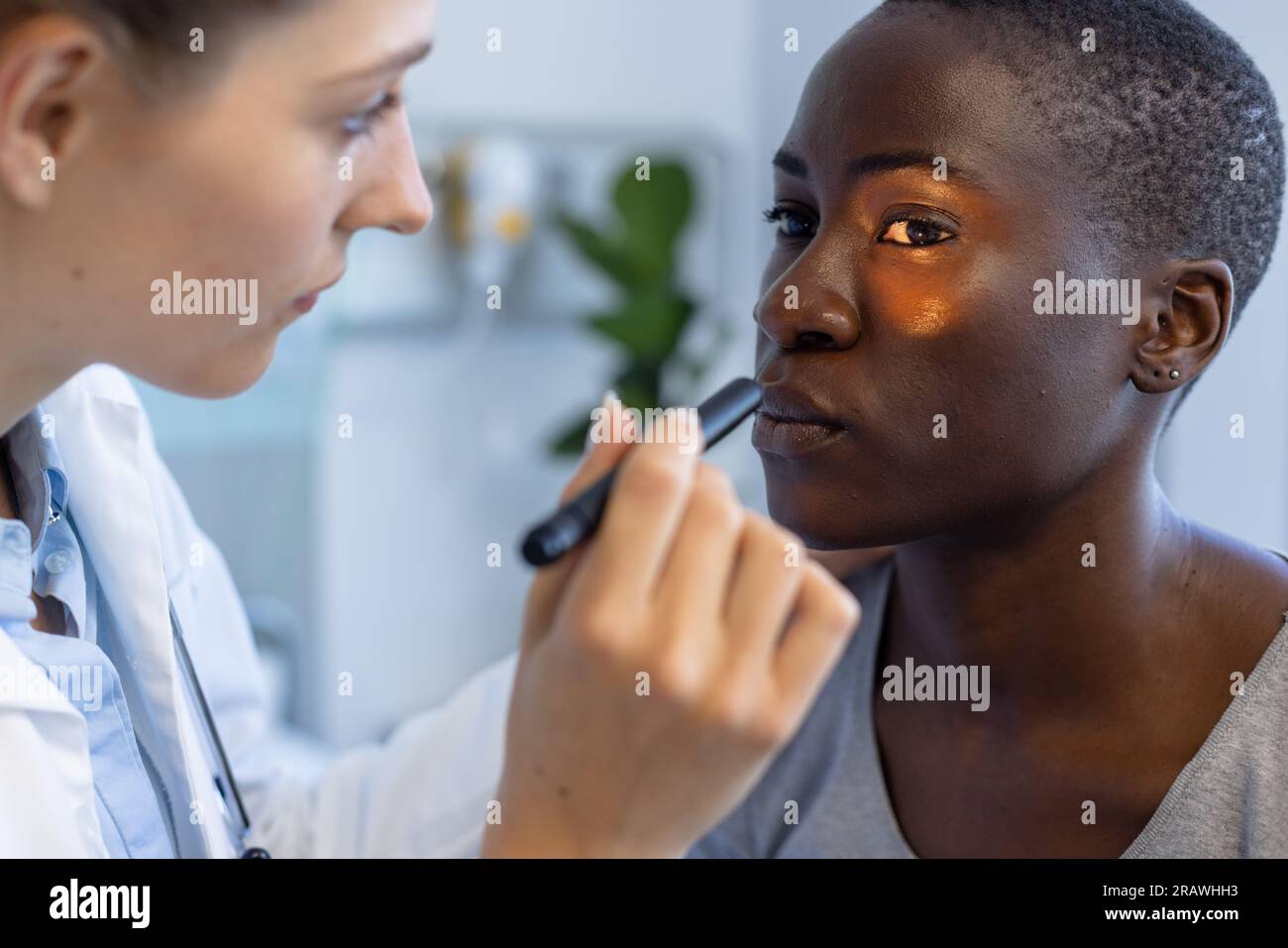 Diverse female doctor and patient examining patient, using flashlight ...