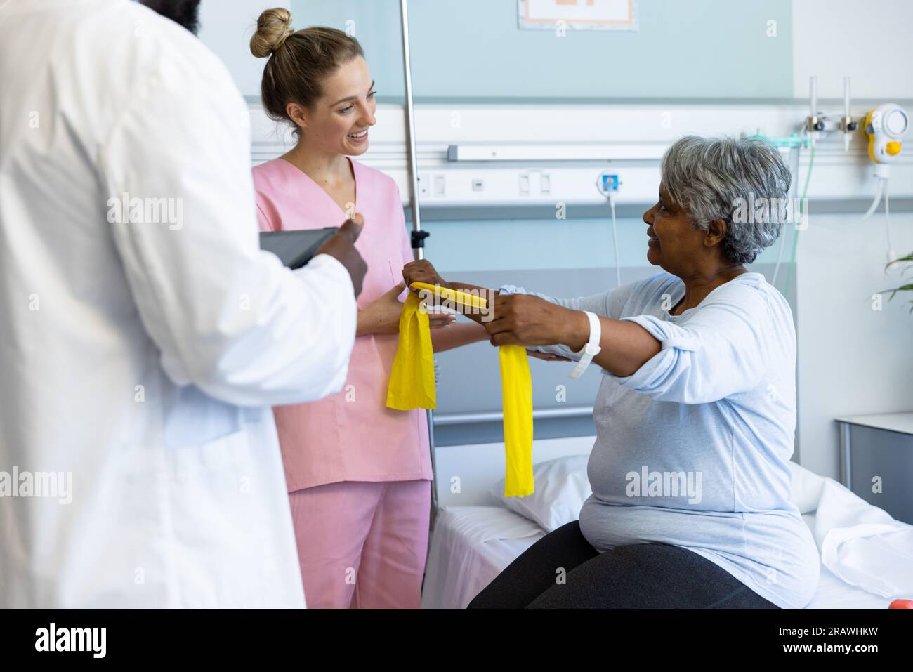 Diverse doctors and senior female patient exercising with tape at ...