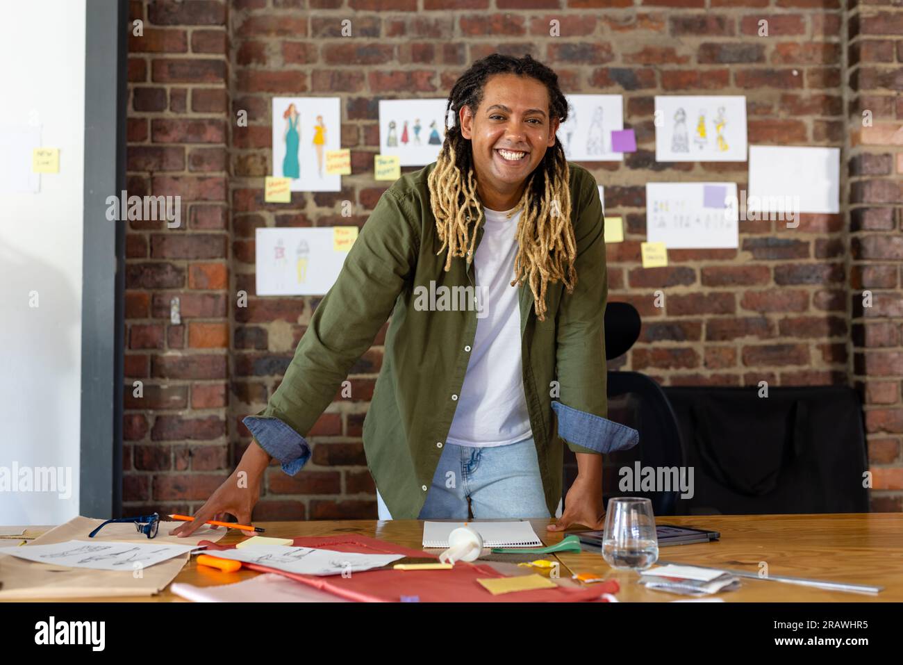 Portrait of biracial male fashion designer with dreadlocks leaning on ...