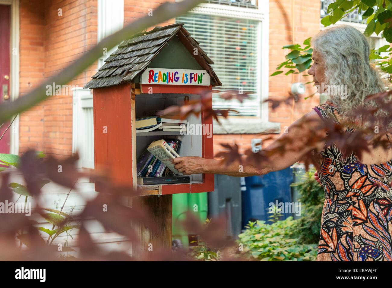 A woman checks out free books at a front yard 'Little Library,' which ...
