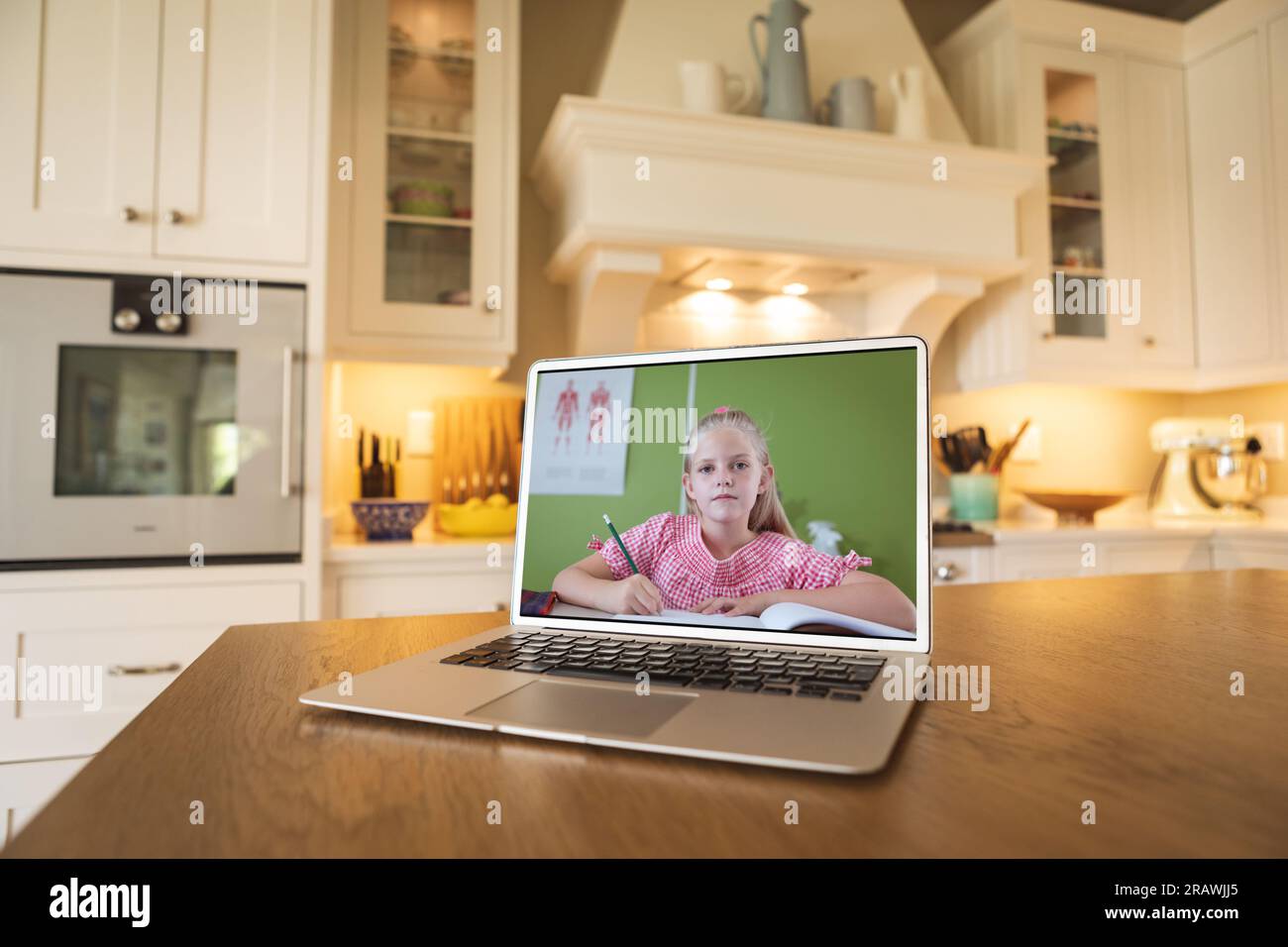 Laptop screen on table with caucasian schoolgirl writing in book while ...