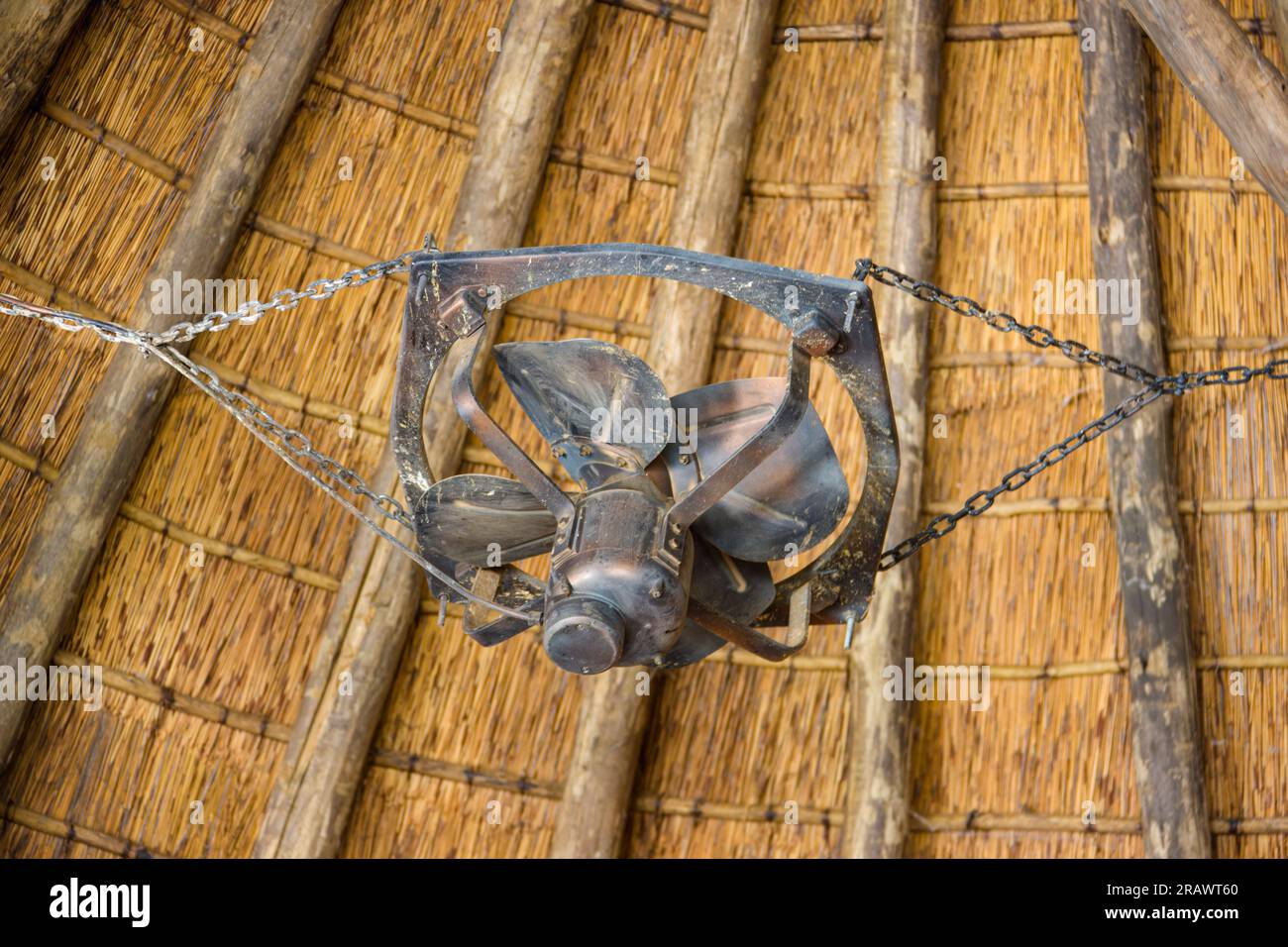 vintage metallic industrial fan on a thatched roof with large wooden ...