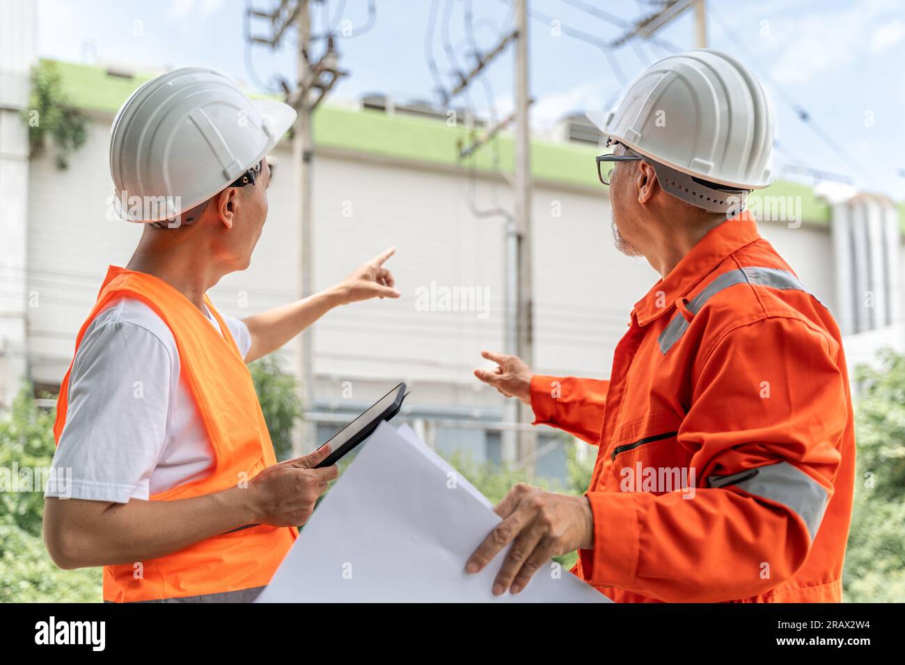 Back view of 2 male engineers or foremen in orange jumpsuit, safety ...