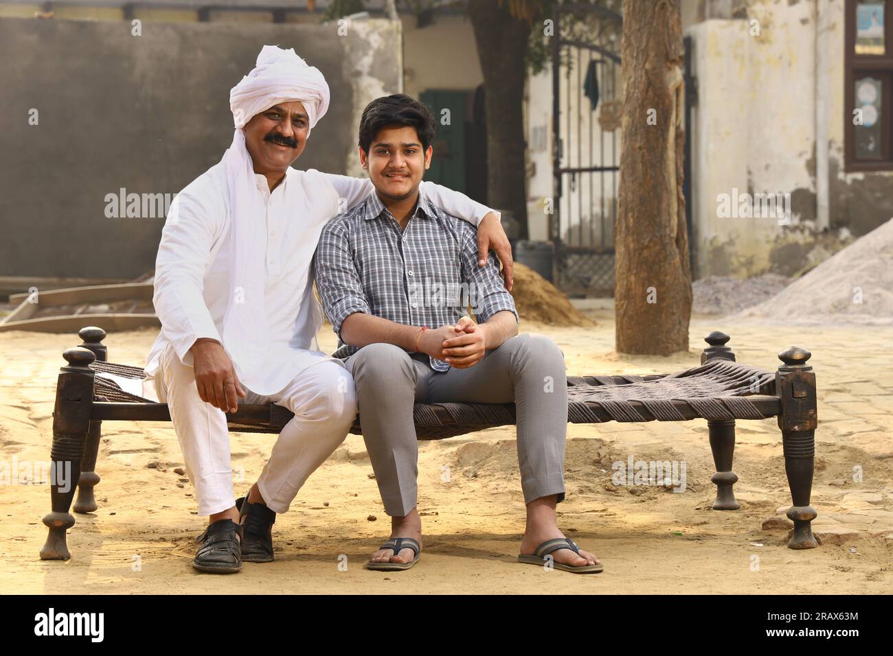 Happy and proud Indian Father sitting with his son on a cot looking ...