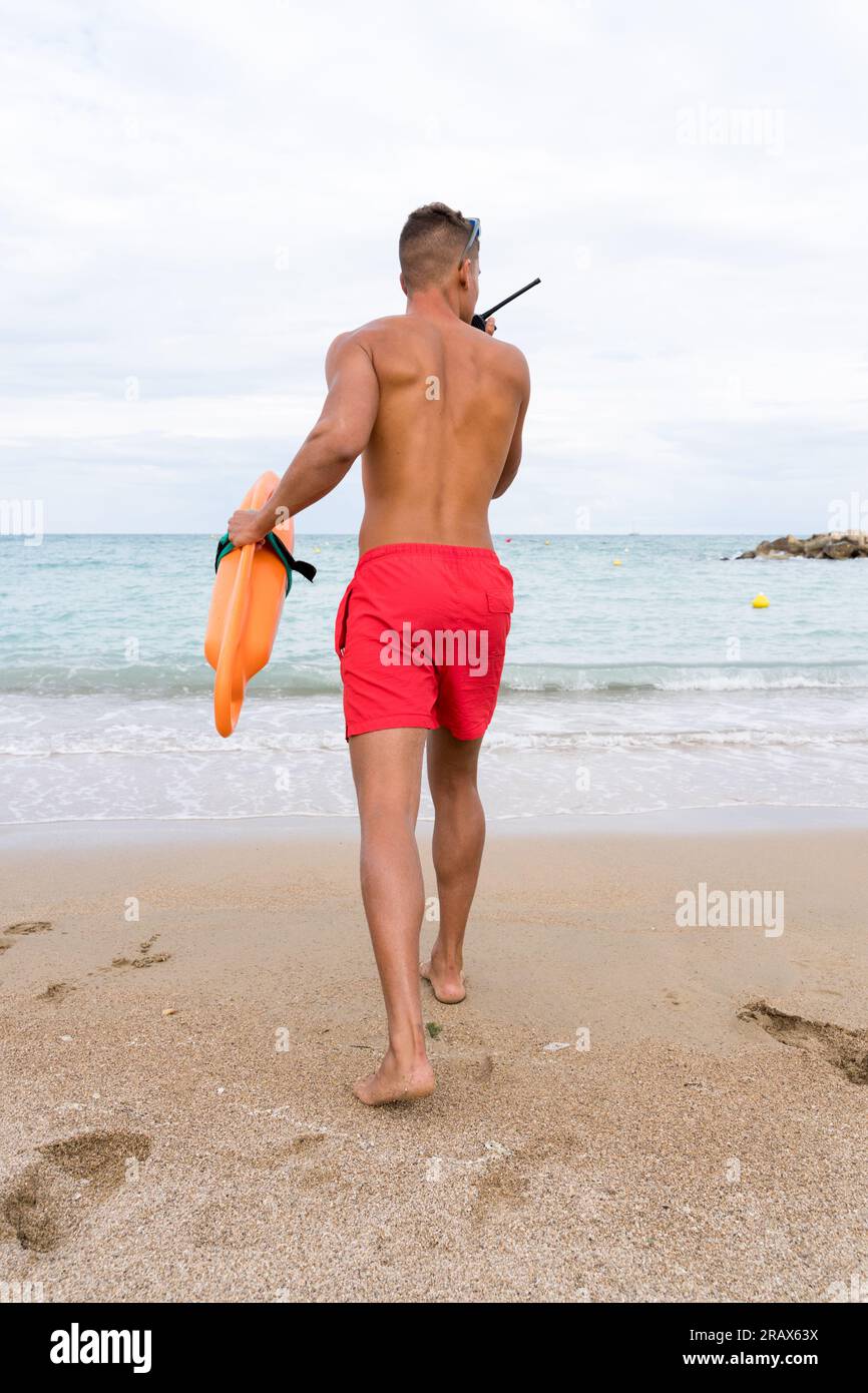 Vertical photo of the rear view of a Lifeguard using the radio while ...