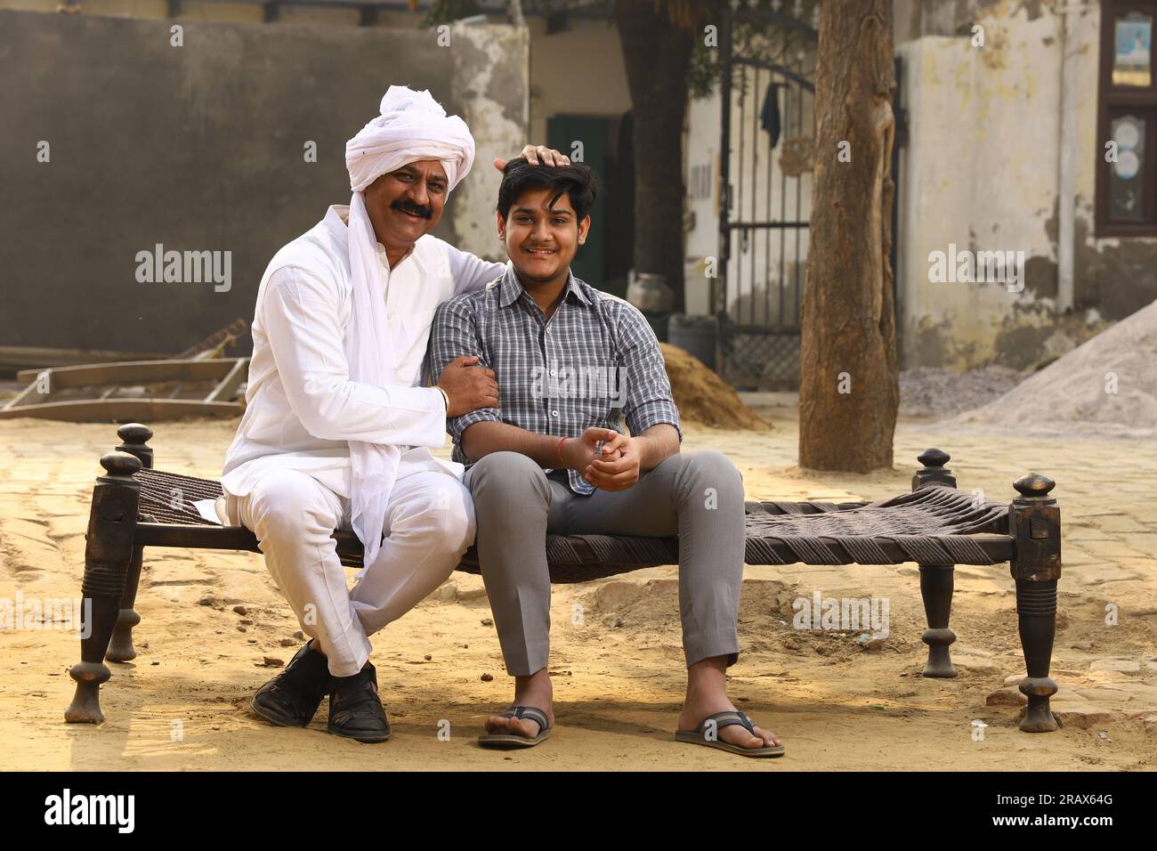 Happy and proud Indian Father sitting with his son on a cot looking ...
