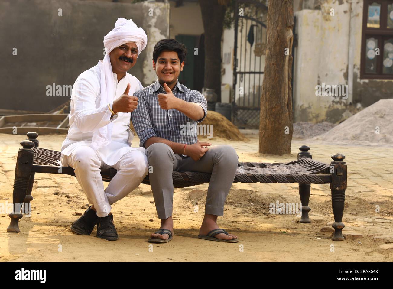 Happy and proud Indian Father sitting with his son on a cot looking ...