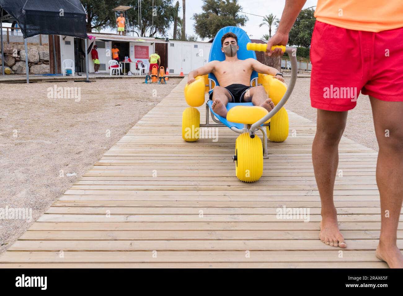 lifeguard dragging an injured man with a chair with wheels on the beach ...