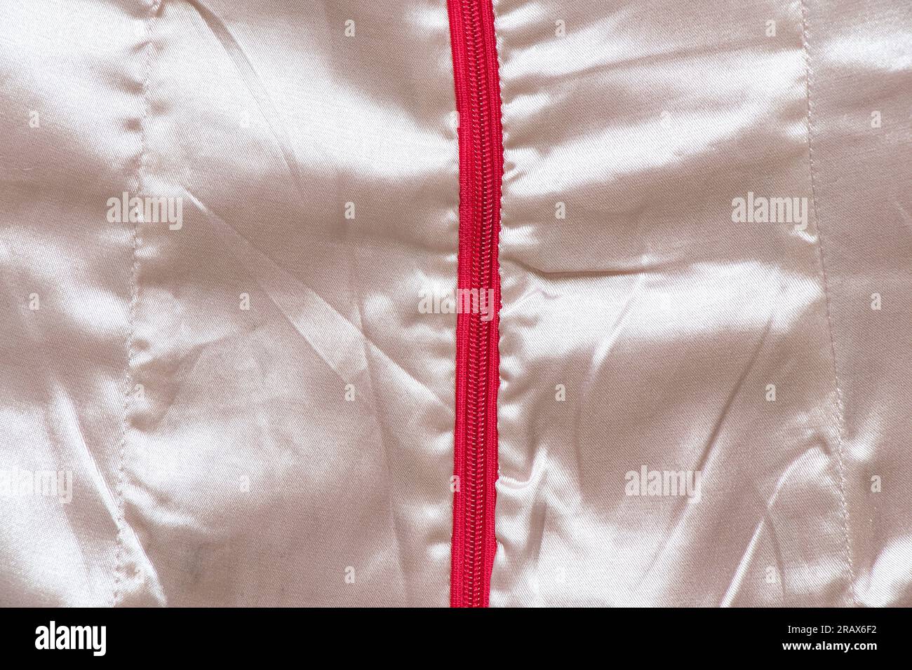 white wrinkled silk fabric as background close-up with red zipper in ...