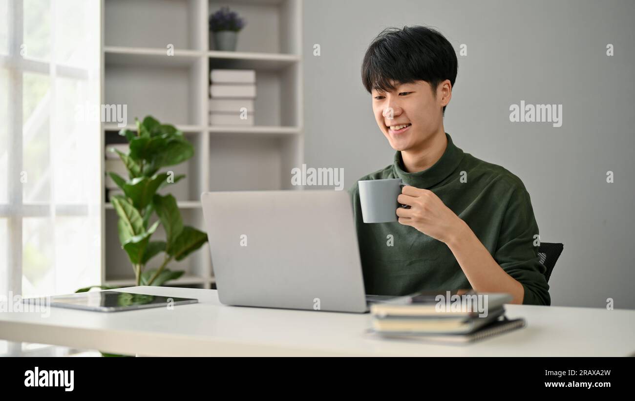 A smart and handsome Asian man sipping coffee while working on his ...