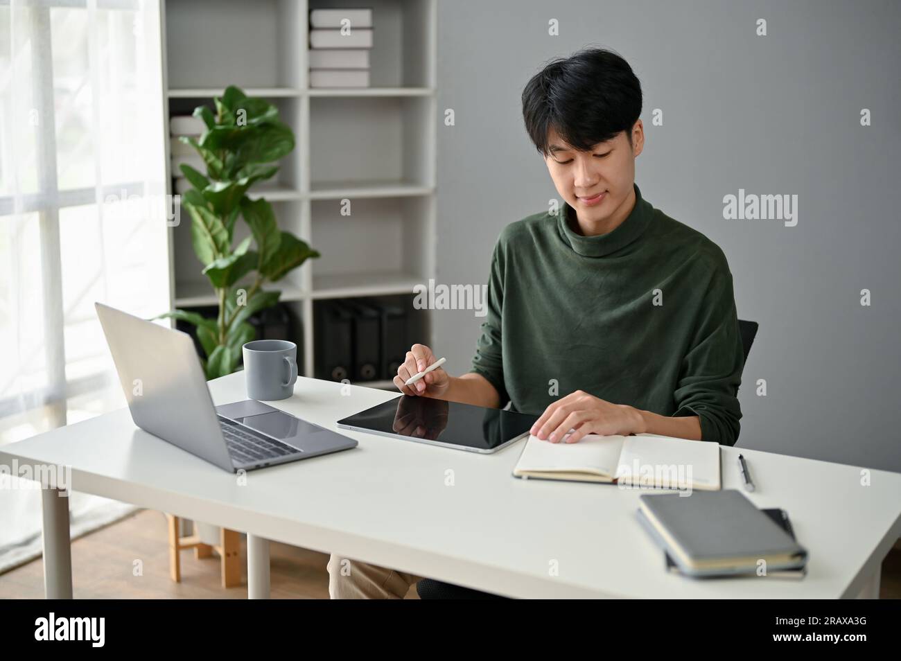 A handsome and focused Asian man in casual clothes working on his tasks ...