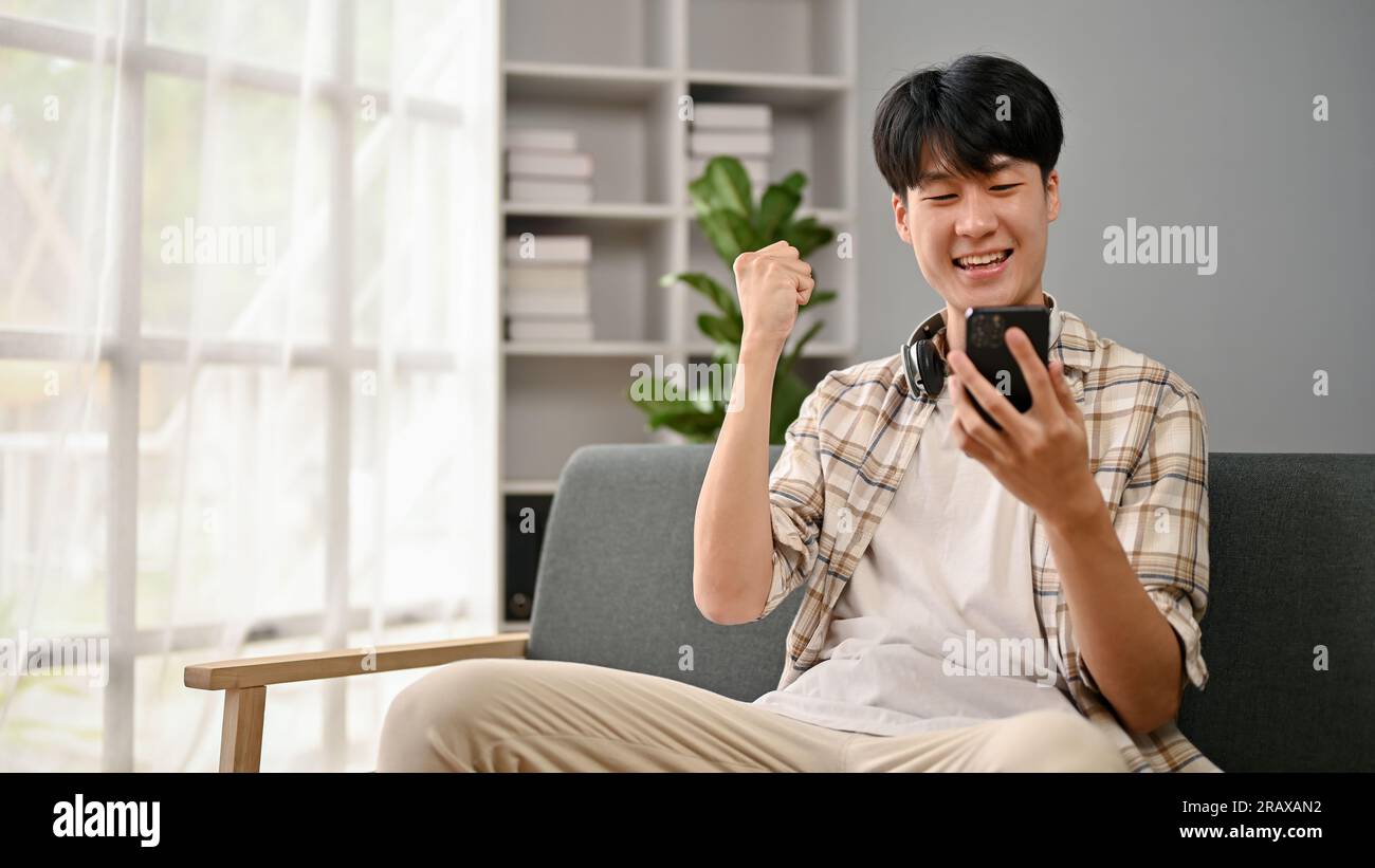 A happy and smiling young Asian man in casual clothes looking at his ...