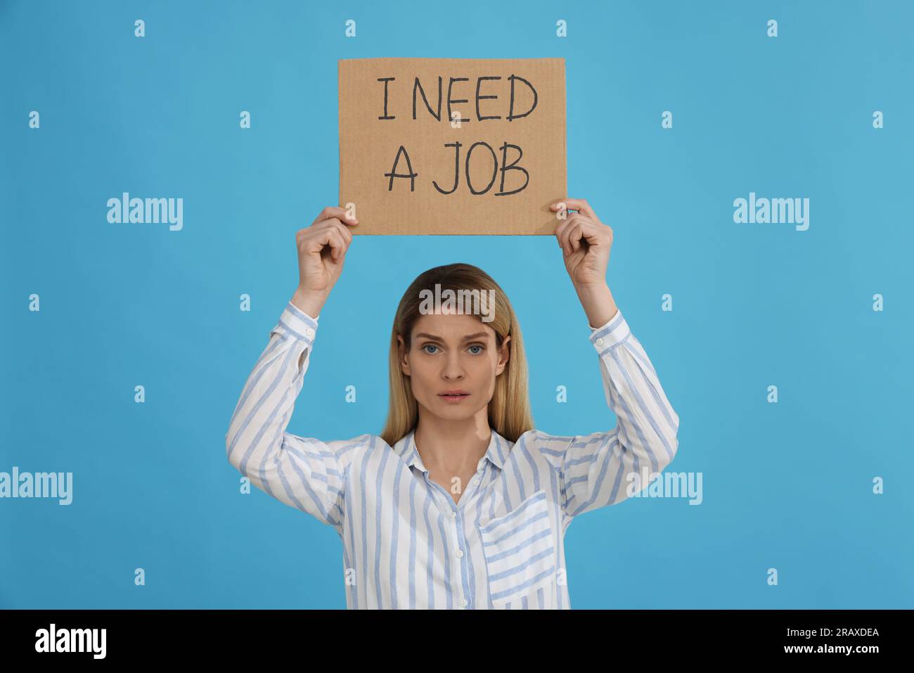 Unemployed woman holding sign with phrase I Need A job on light blue ...