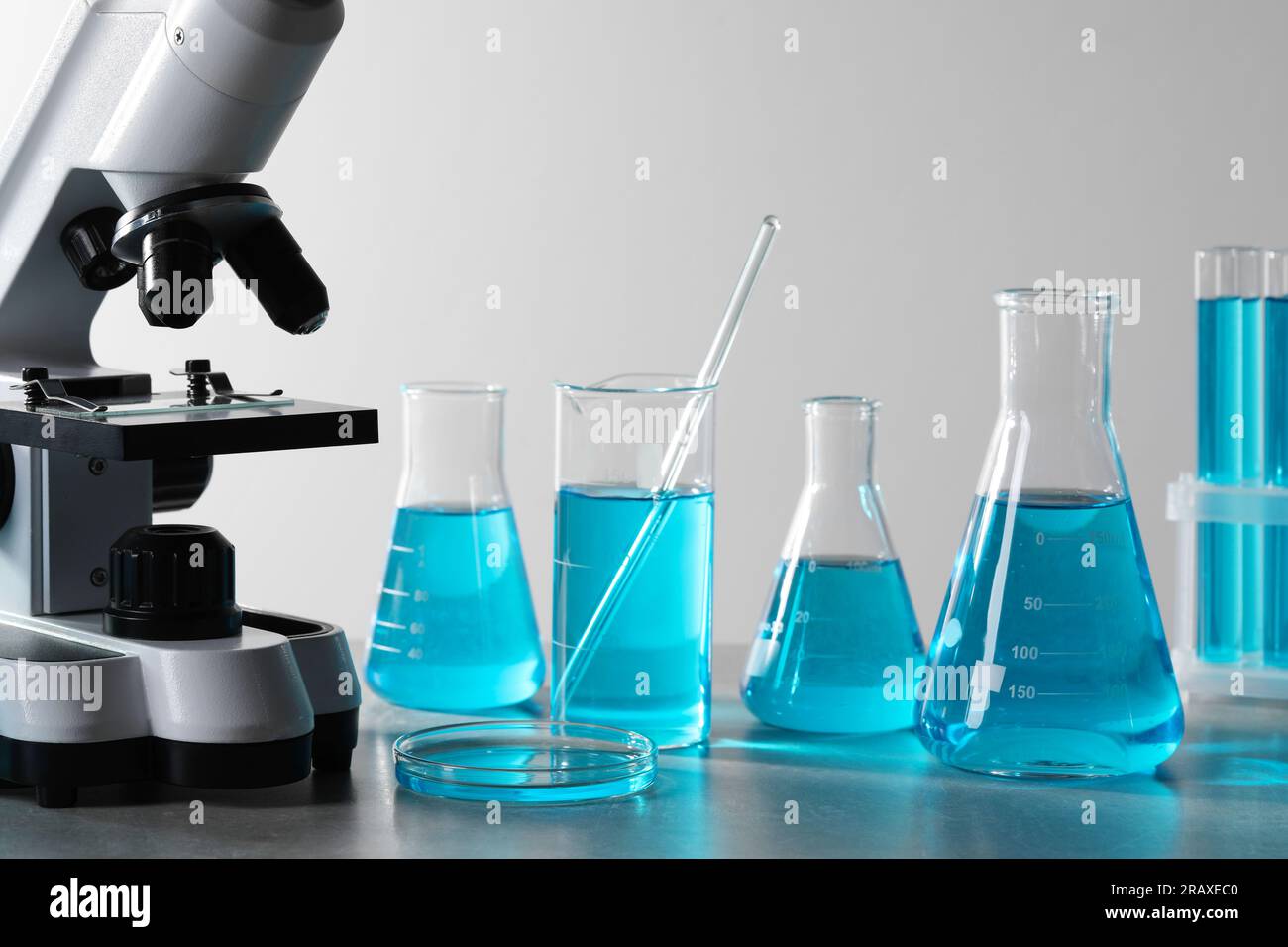 Different laboratory glassware with light blue liquid and microscope on ...