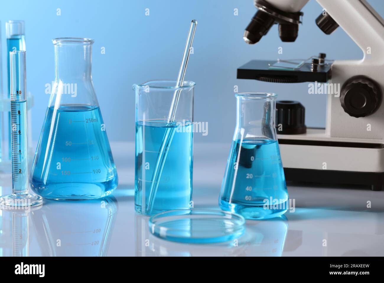 Different laboratory glassware with light blue liquid and microscope on ...