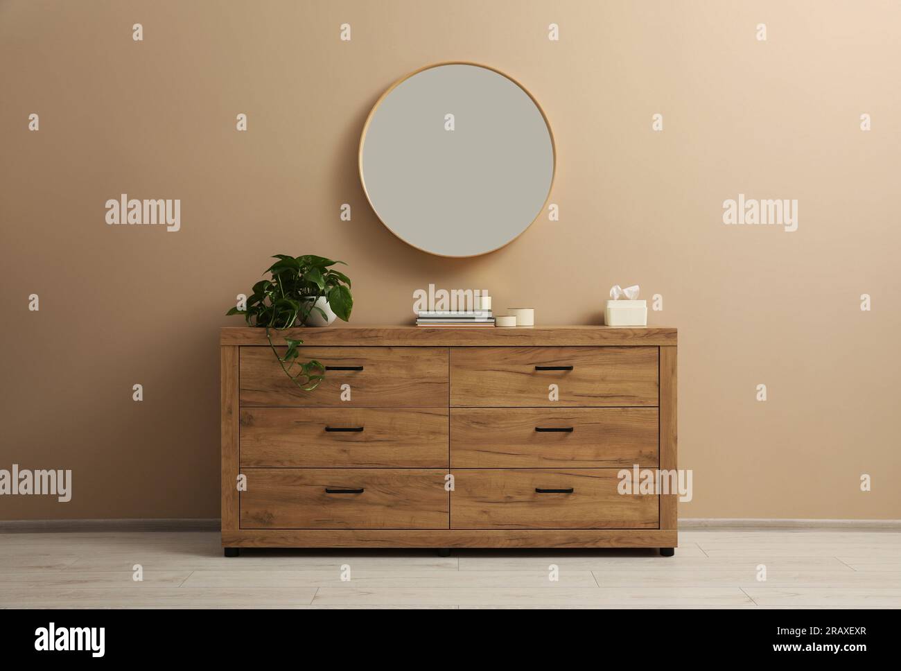 Wooden stylish chest of drawers near light brown wall with round mirror ...