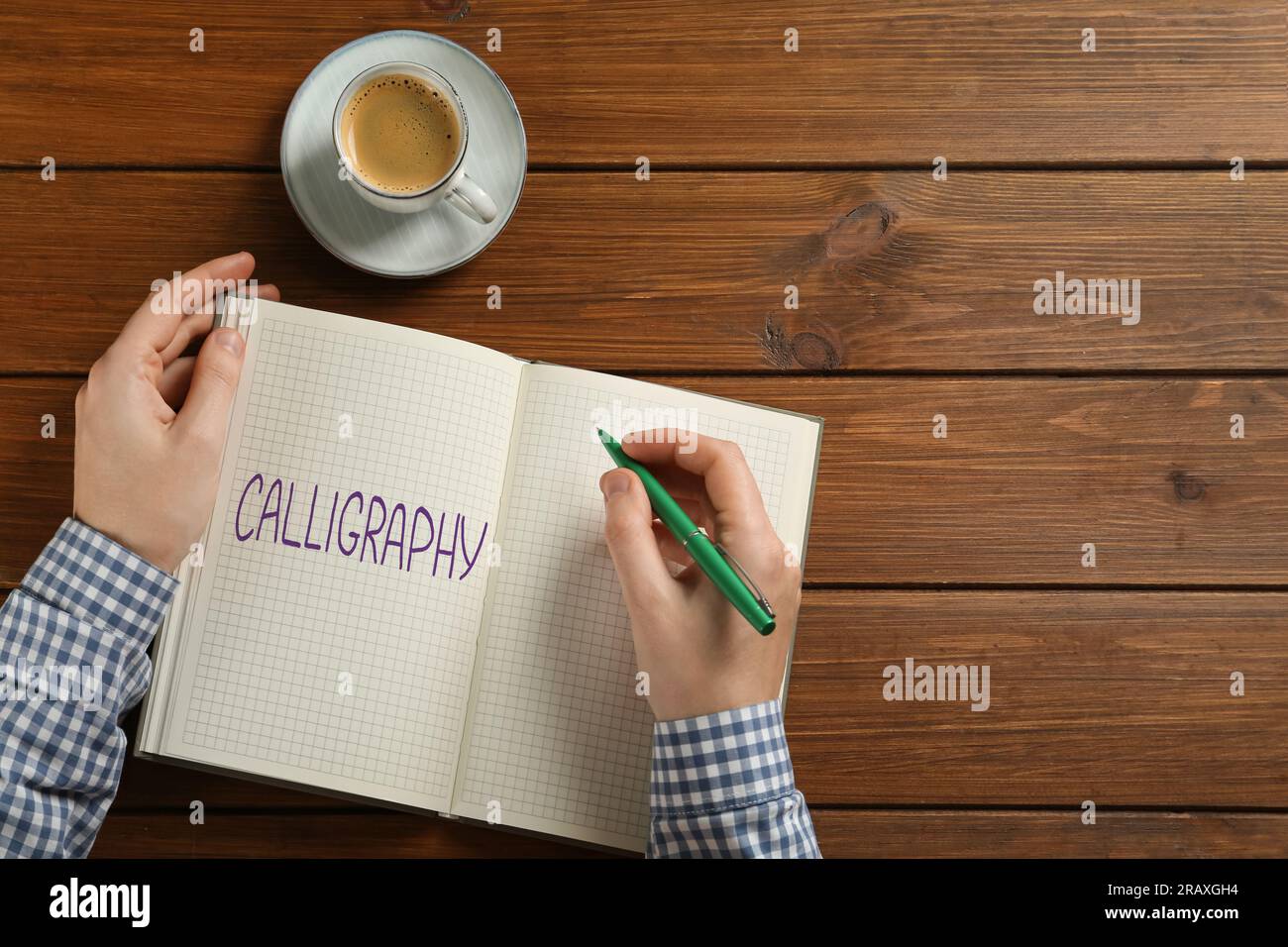 Man writing word Calligraphy in notebook at wooden table, top view ...