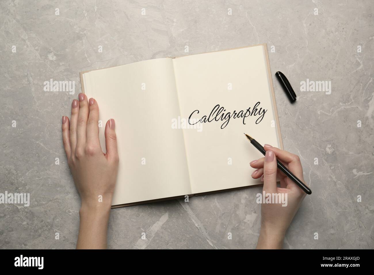 Woman writing word Calligraphy in notebook at grey marble table, top ...