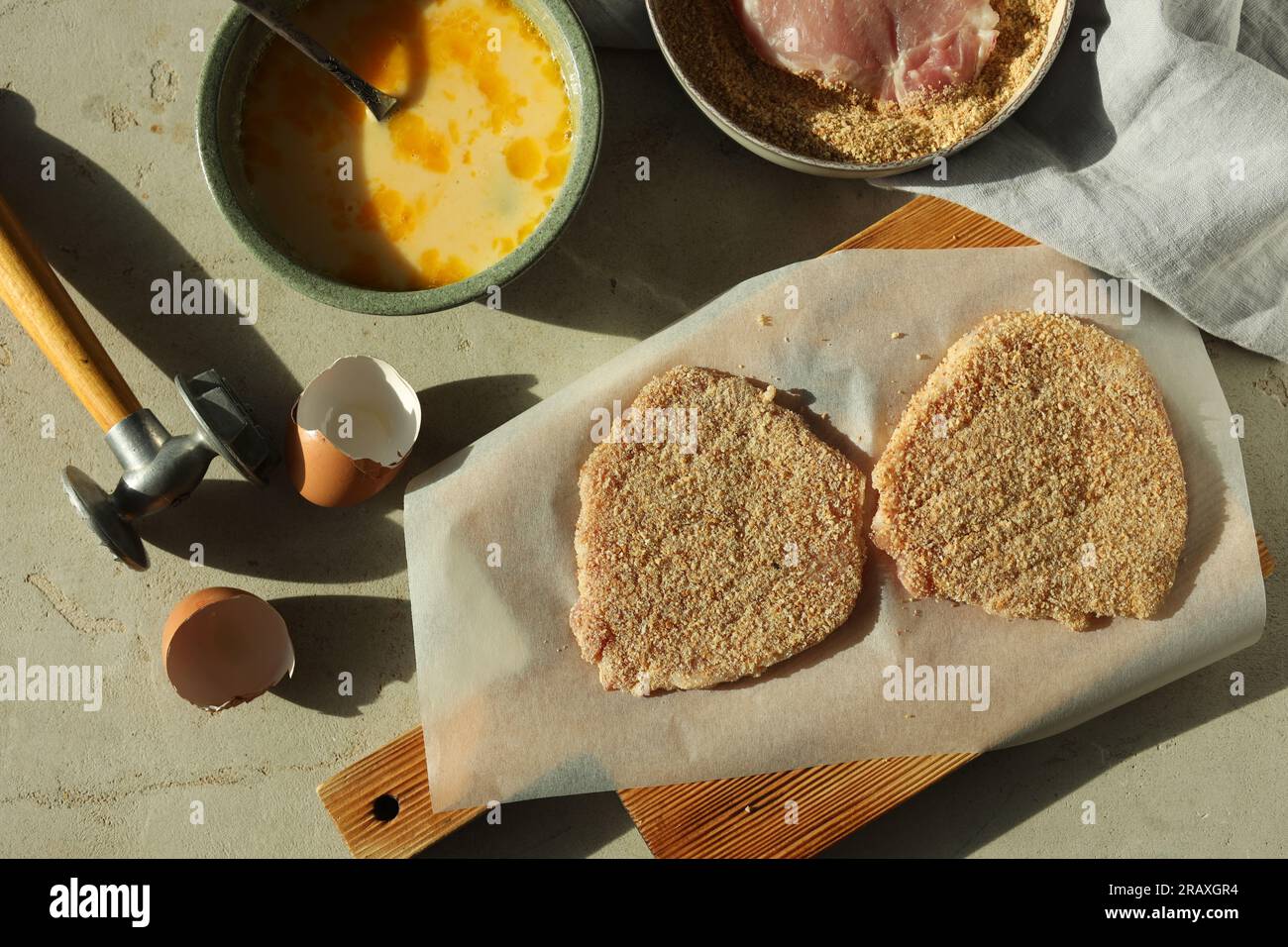 Cooking schnitzel. Raw pork chops in bread crumbs, meat mallet and ...