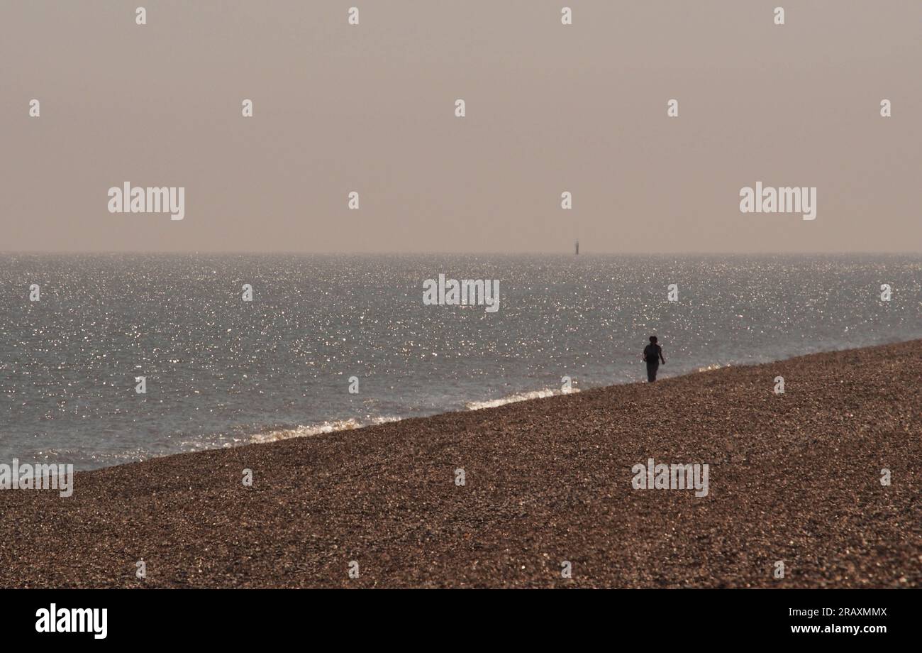 A silouette of a man walking by the sea on the shingle beach at ...