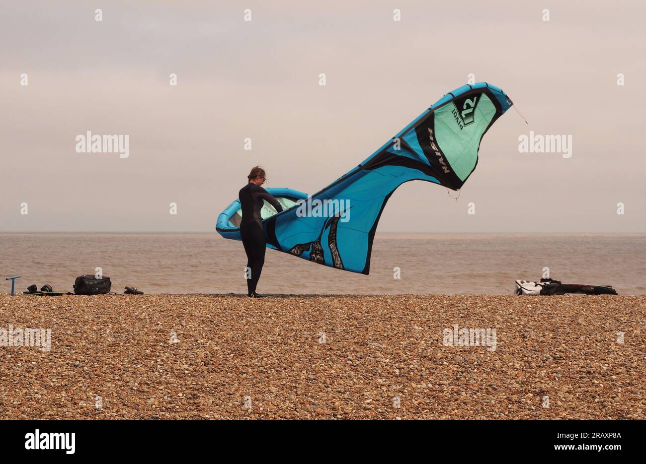 A female windsurfer standing on the shingle beach at Aldeburgh, Suffolk ...