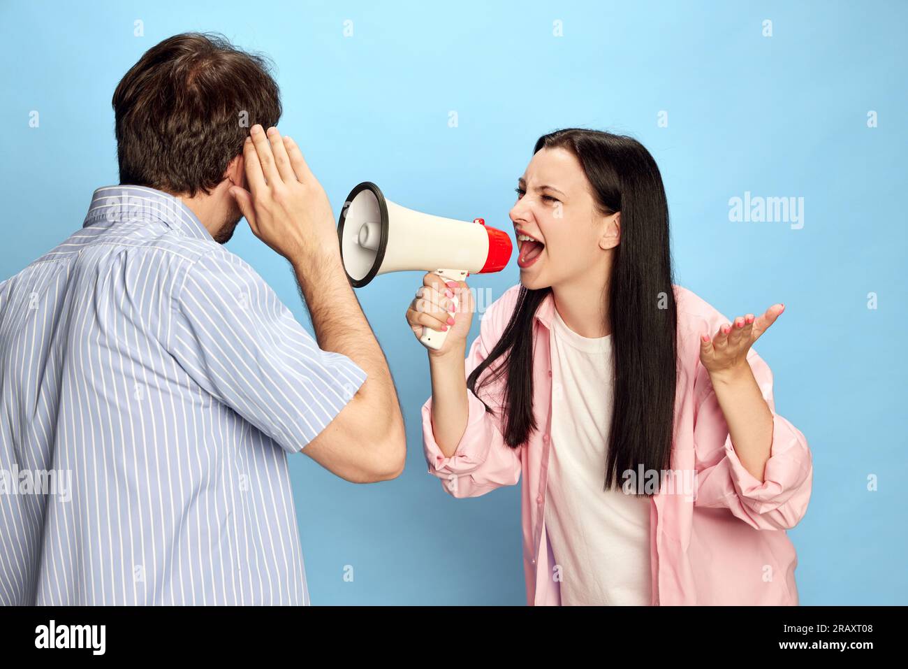 Woman shouting in megaphone to man against blue studio background ...