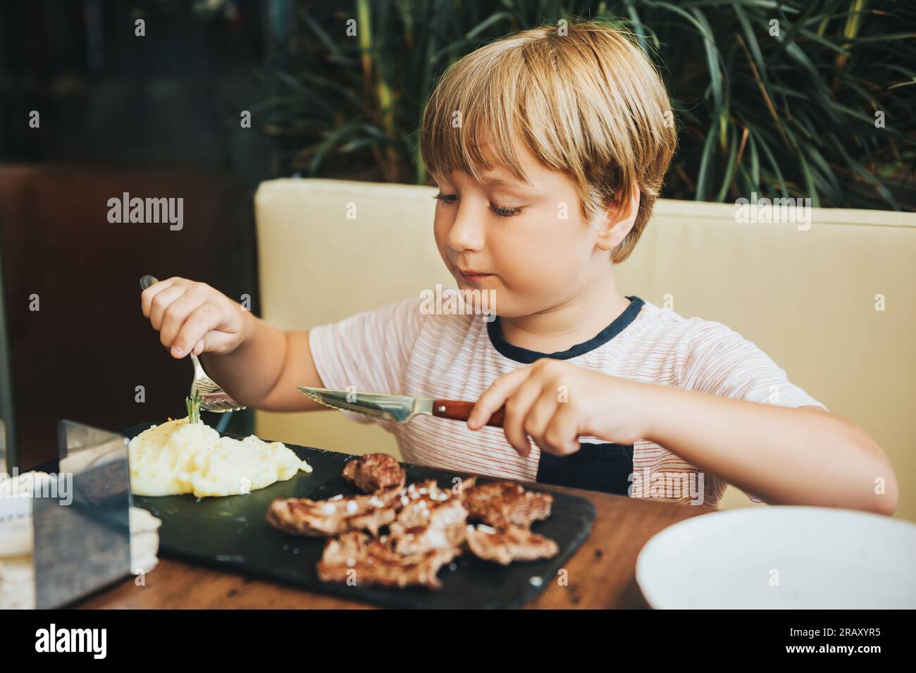 Cute little boy eating steak and mashed potatoes in the restaurant ...