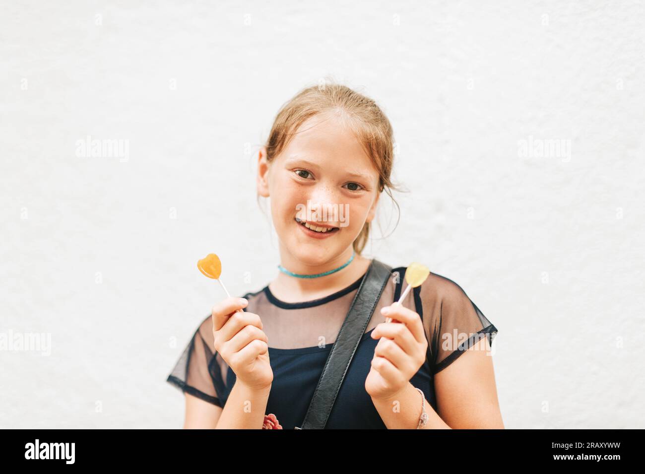 Outdoor portrait of cute kid girl holding heart shaped lollipop candies ...