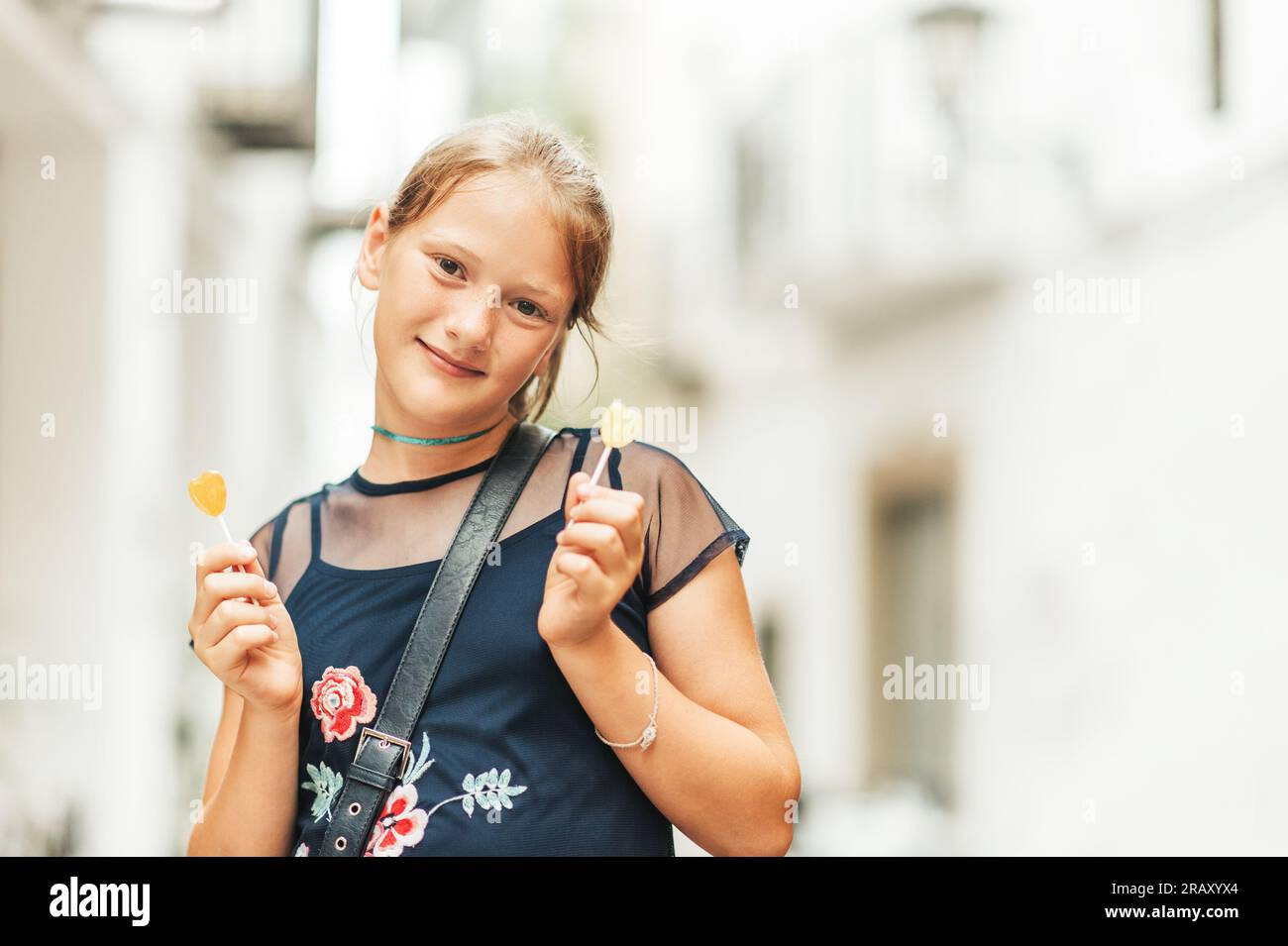 Outdoor portrait of cute kid girl holding heart shaped lollipop candies ...