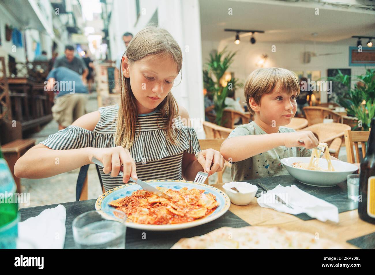 Two funny kids having lunch in the restaurant, eating ravioli and pasta ...
