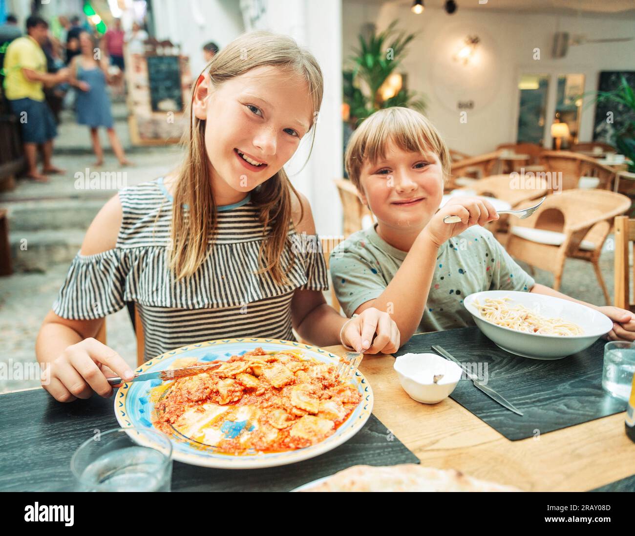 Two funny kids having lunch in the restaurant, eating ravioli and pasta ...