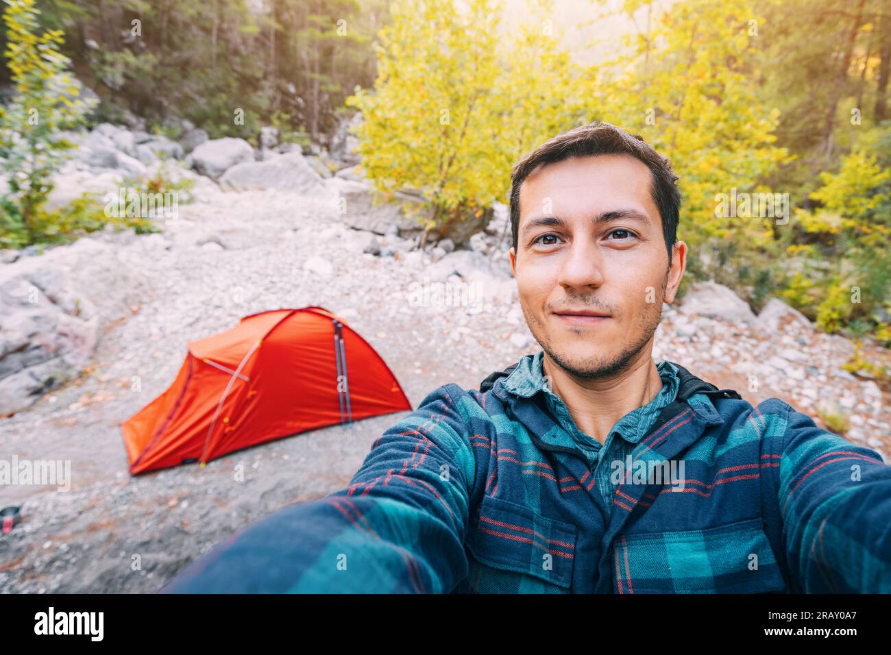 Happy hiker man taking selfie photo against red tent in the woods. Solo ...