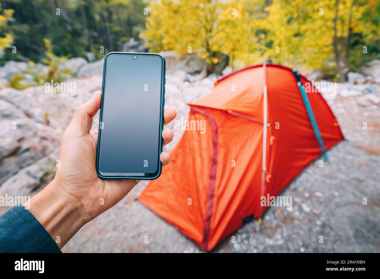 Smartphone in hand against background camping tent. Hiking and internet ...