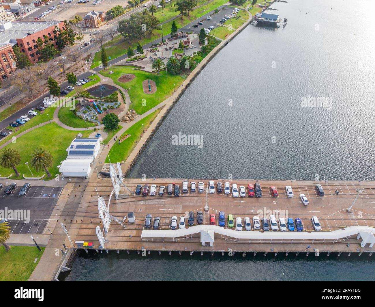 Aerial view of cars parked along a coastal jetty alongside a green ...
