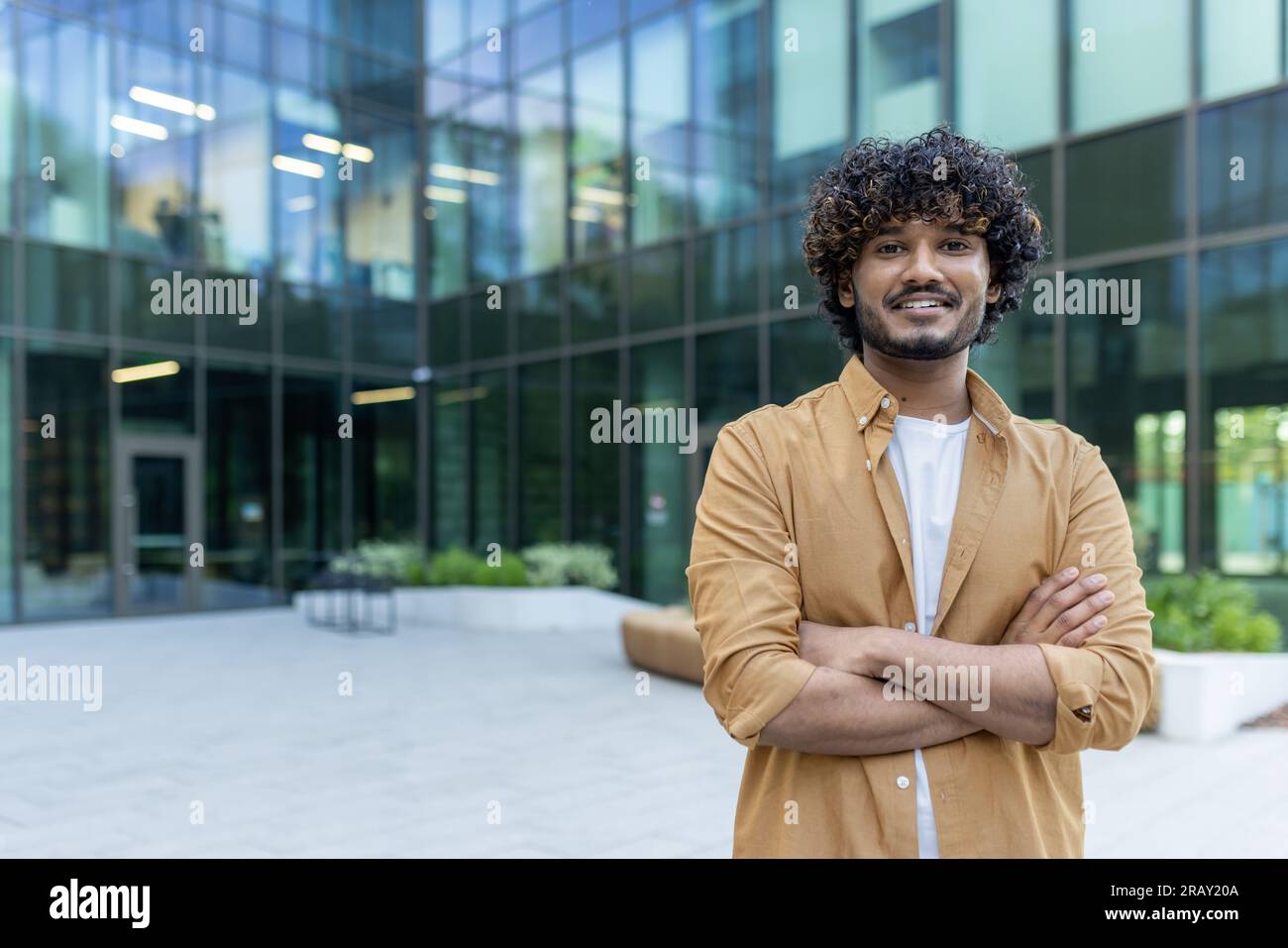Portrait of young confident, handsome and intelligent Indian male student standing outside ...