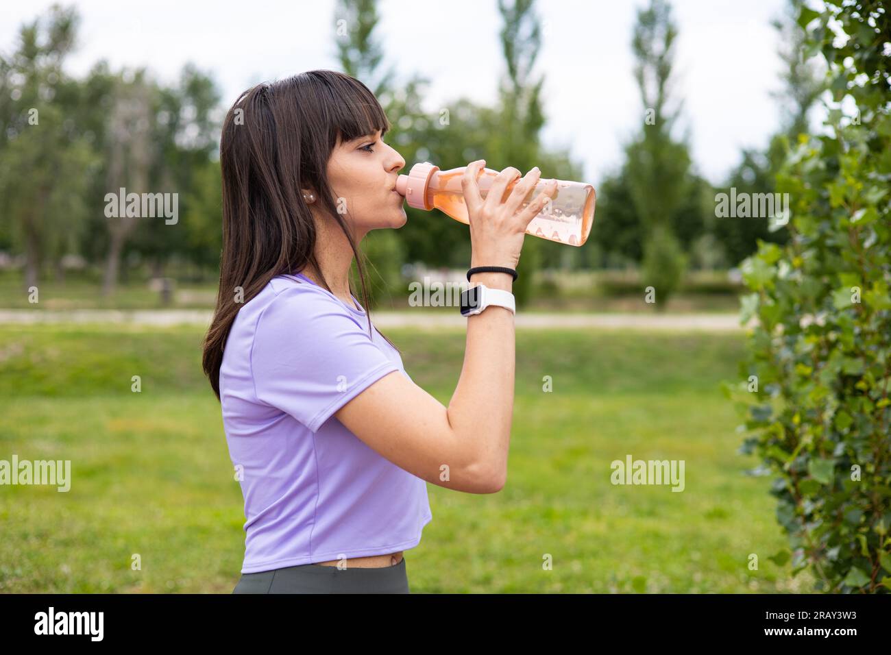 Sport woman drinking after fitness training outdoors. Young female athlete hydrating during ...
