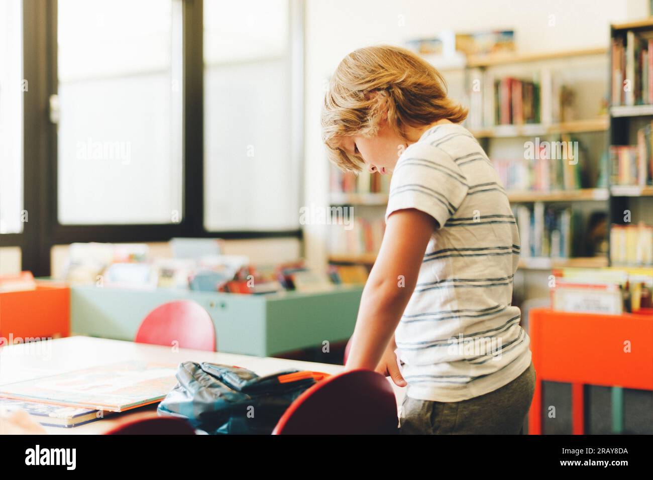 Sweet little boy packing backpack in classroom, education for children ...